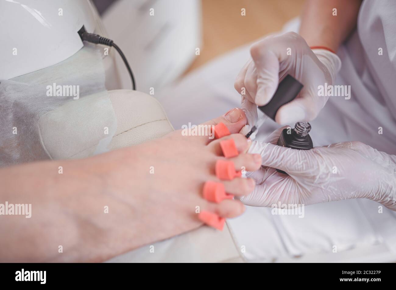 Pedicurist doing white nail polish on client legs using shellac lamp ...