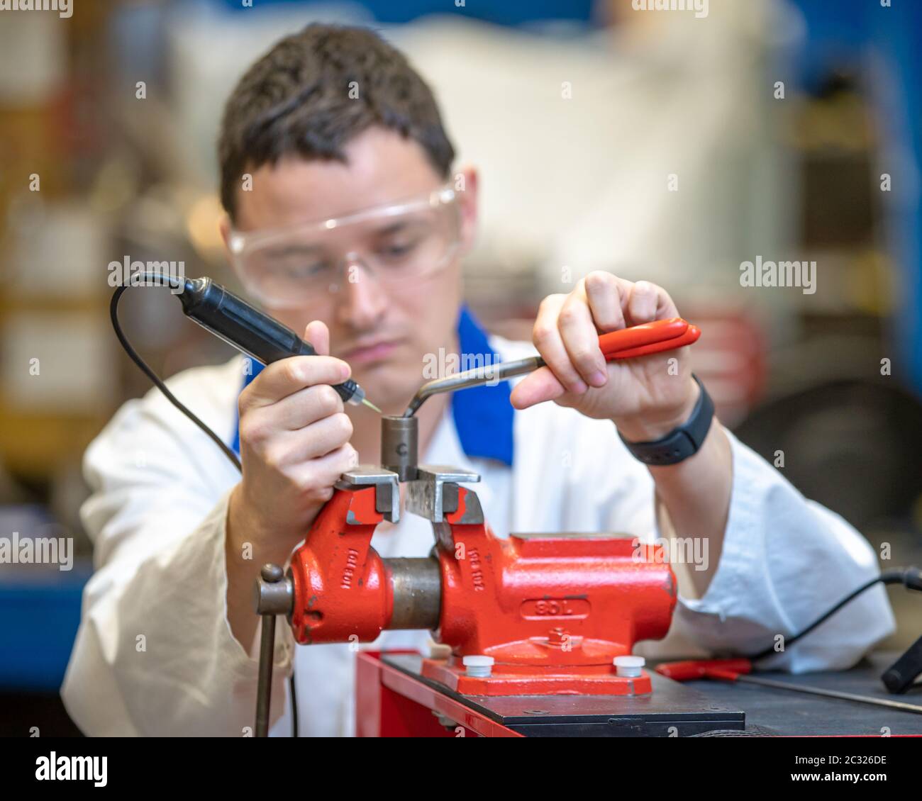 young technician in a factory repairing a machine. man uses a vise to ...