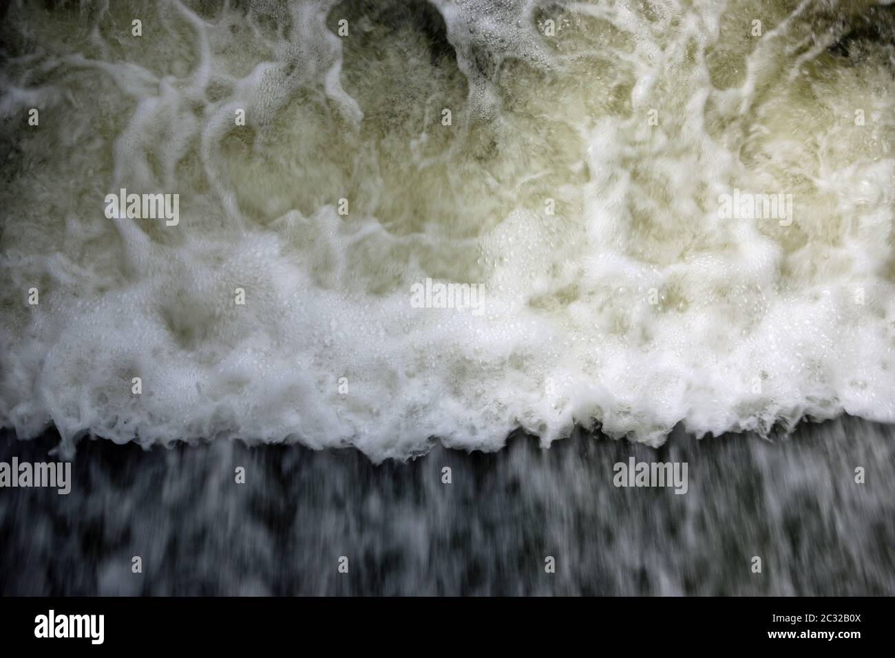 Looking down from above at water flowing over a small weir on a river ...