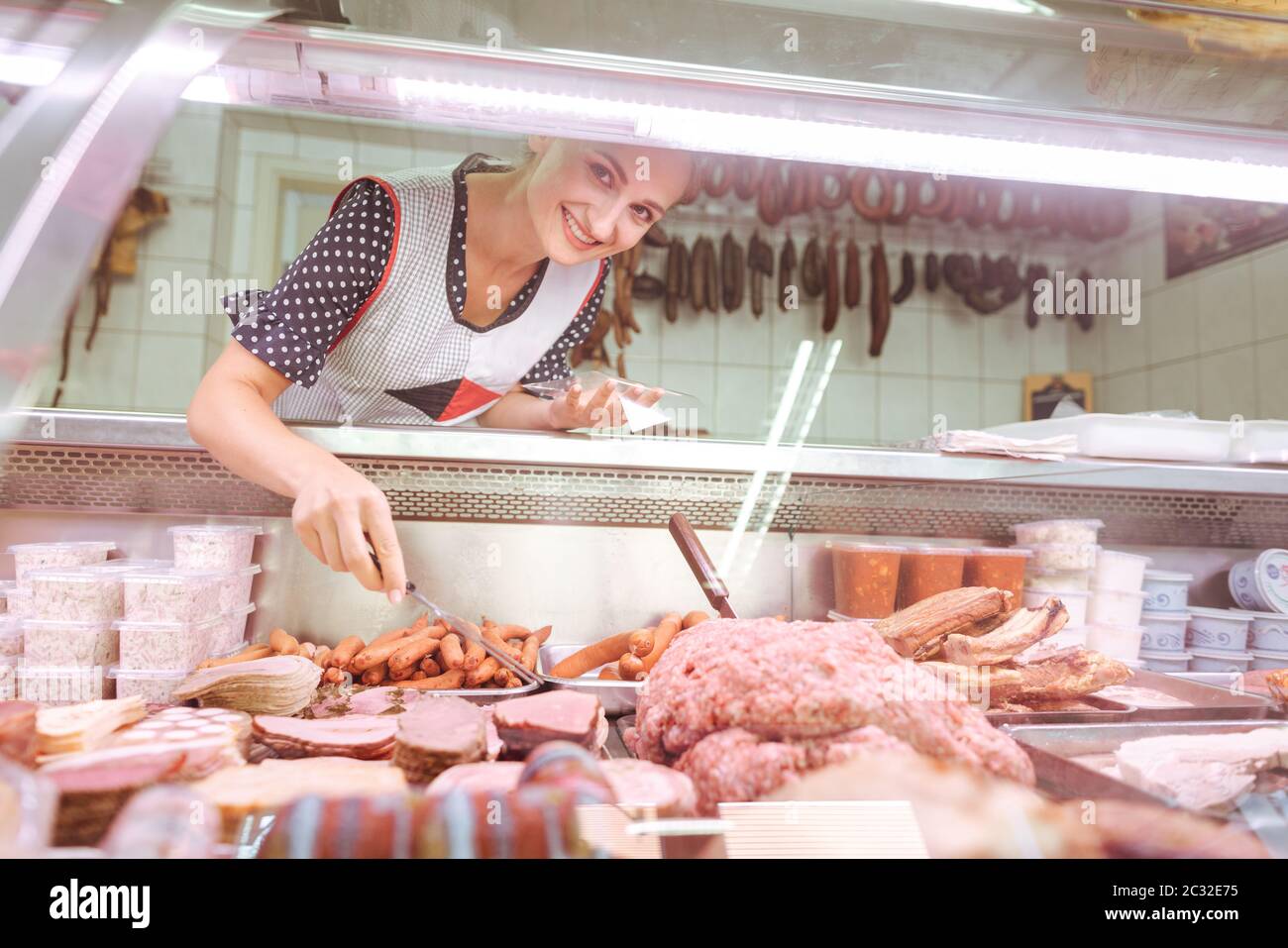 Saleswoman in butchery behind glass display with traditional meat and ...