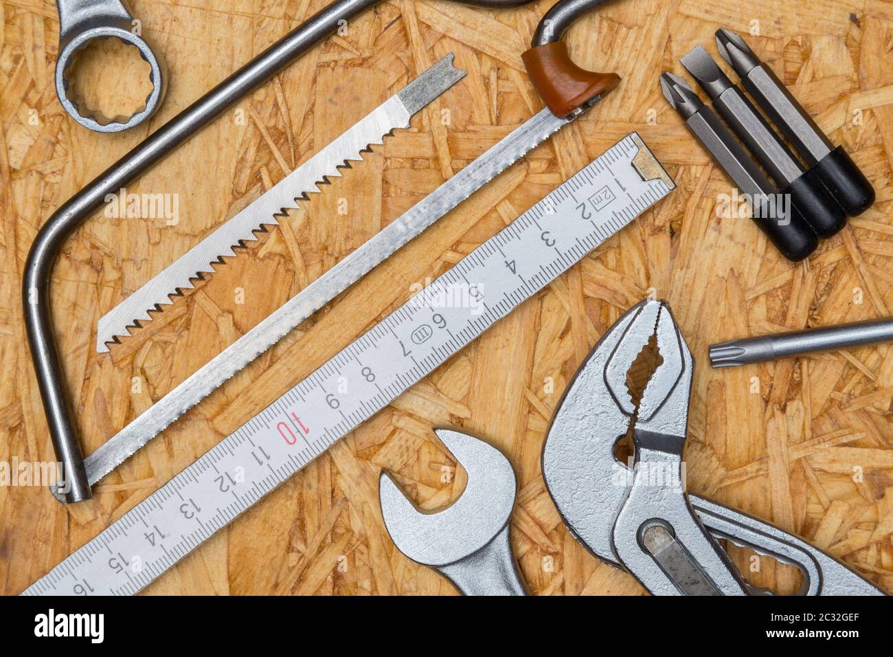 Tool concept, pliers, tine, saw, wrench on wooden plate and bird ...