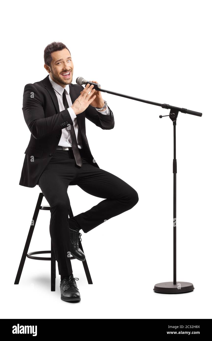 Young man in a suit sitting on a chair and singing on a microphone ...