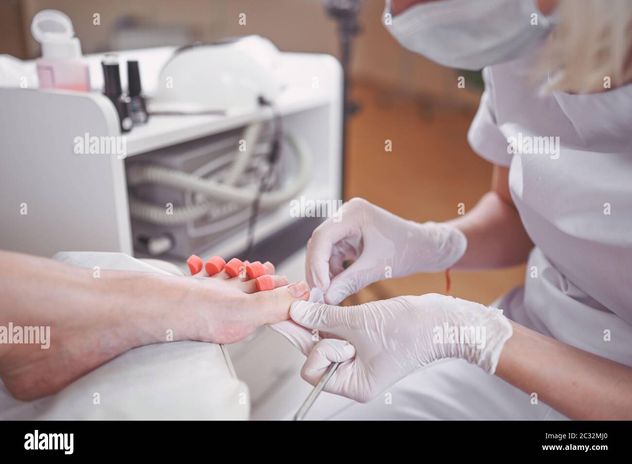 Pedicurist doing white nail polish on client legs using toe finger ...