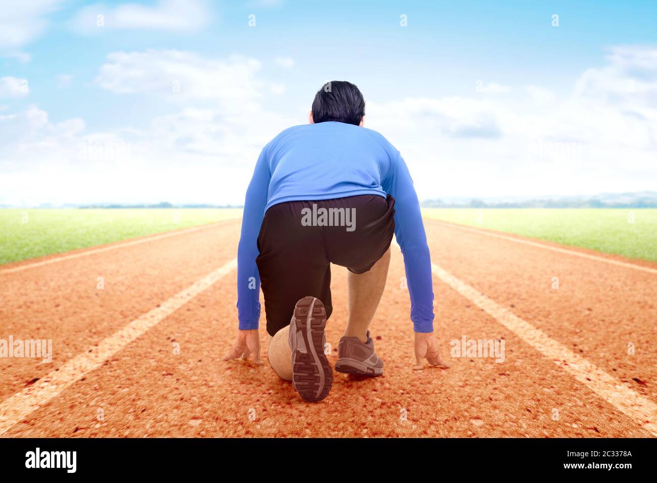Rear view of Asian runner man ready to run on the running track with a ...