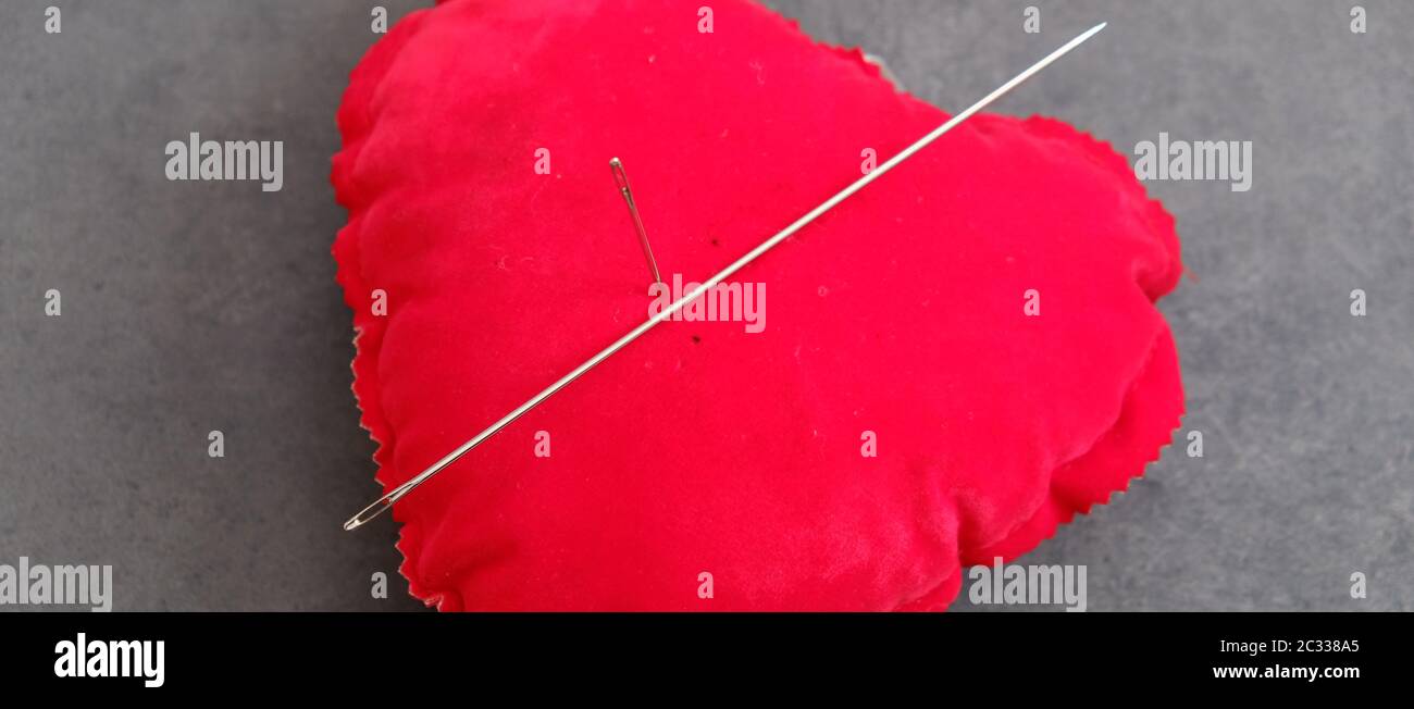 red pincushion and a large sewing needle, needle spell Stock Photo - Alamy