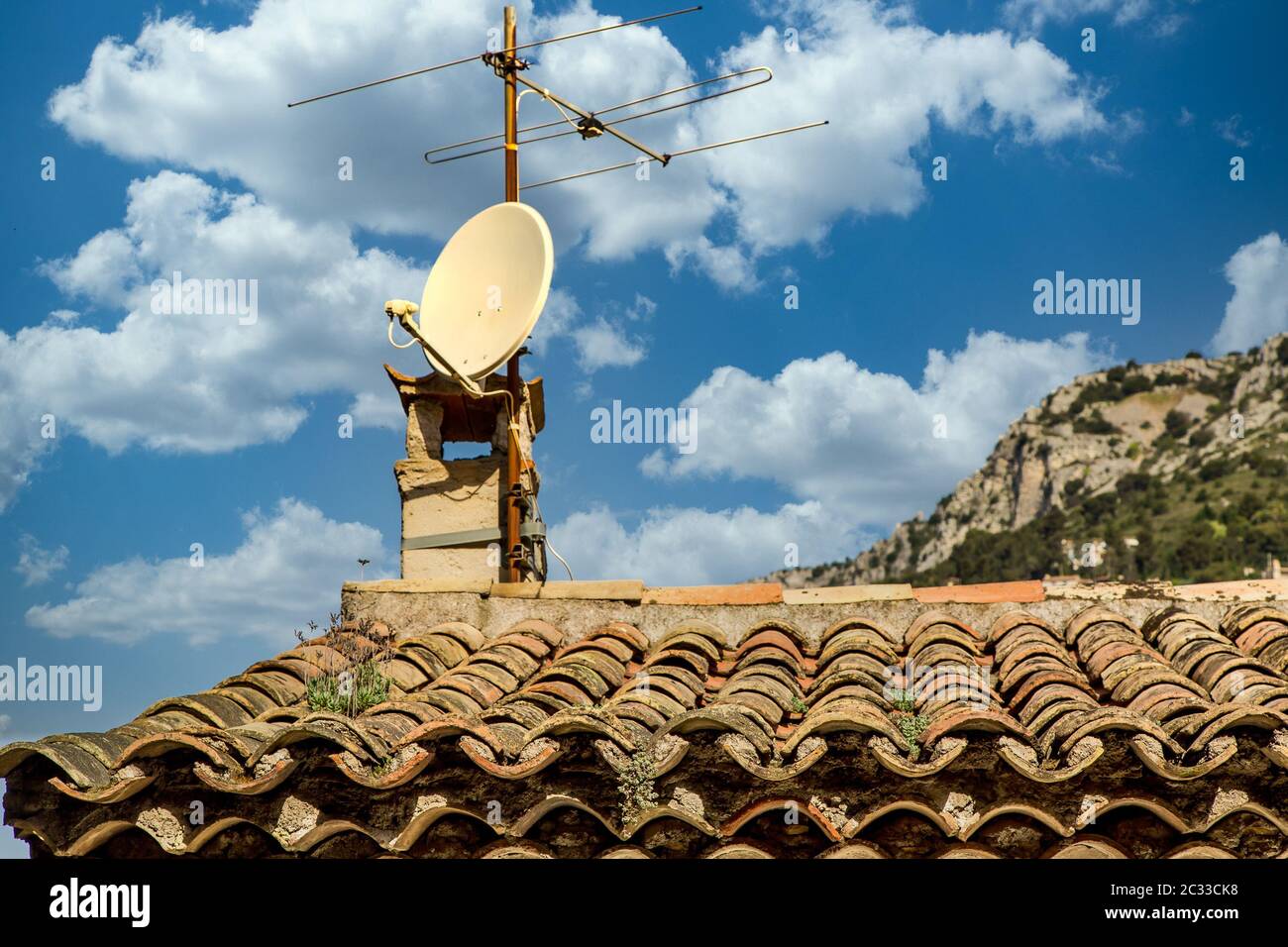 An old Television antenna and a modern TV satellite dish on an old clay ...