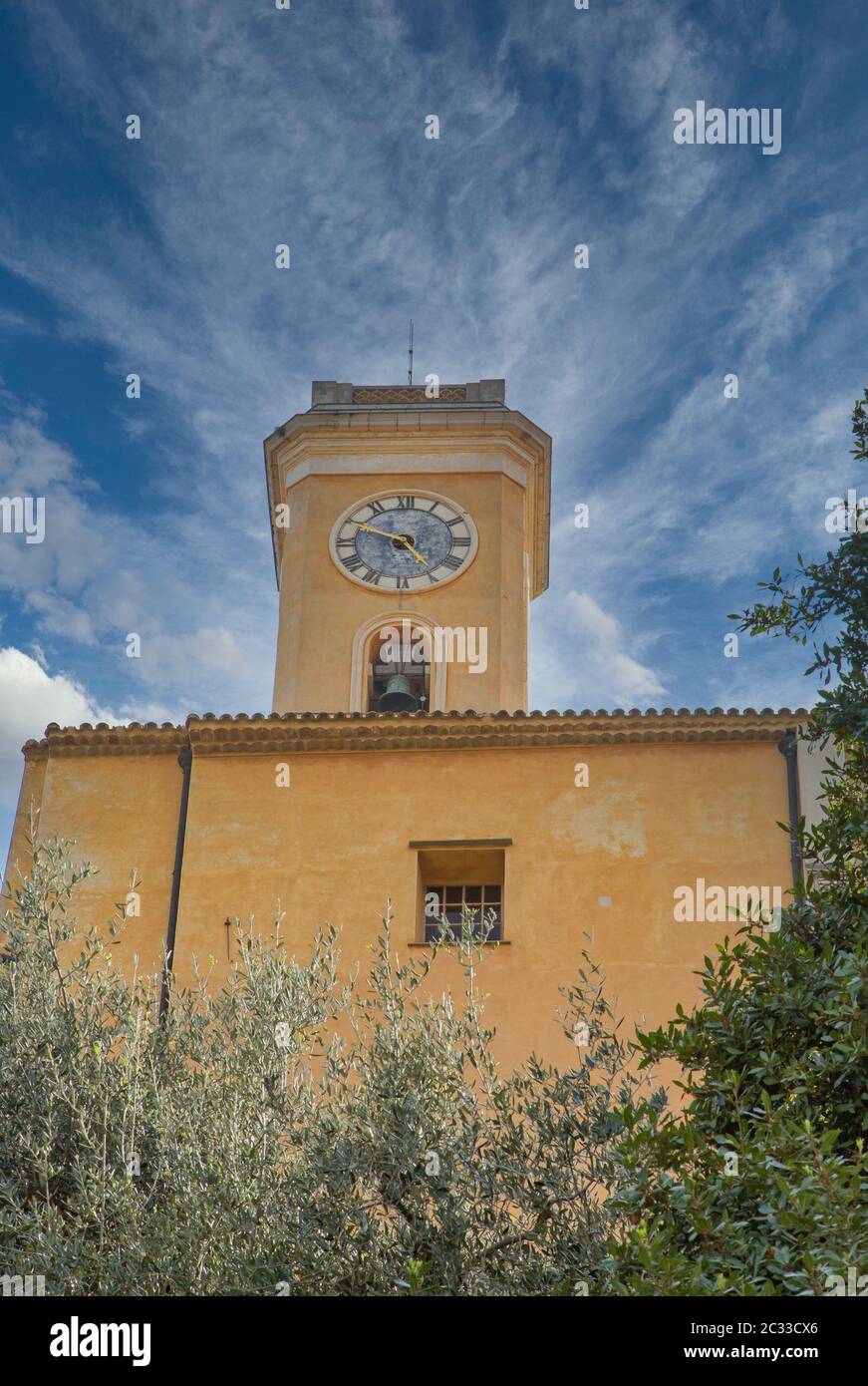 An old yellow plaster clock tower rising from trees on Eze hillside ...