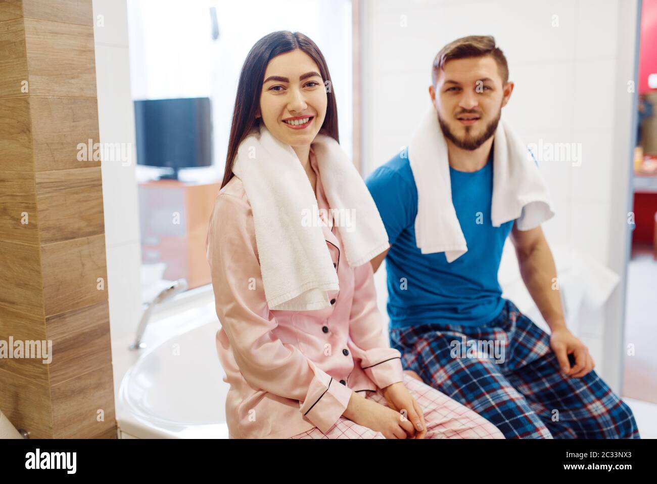 Smiling love couple in pajamas sitting in bathroom at home, morning ...