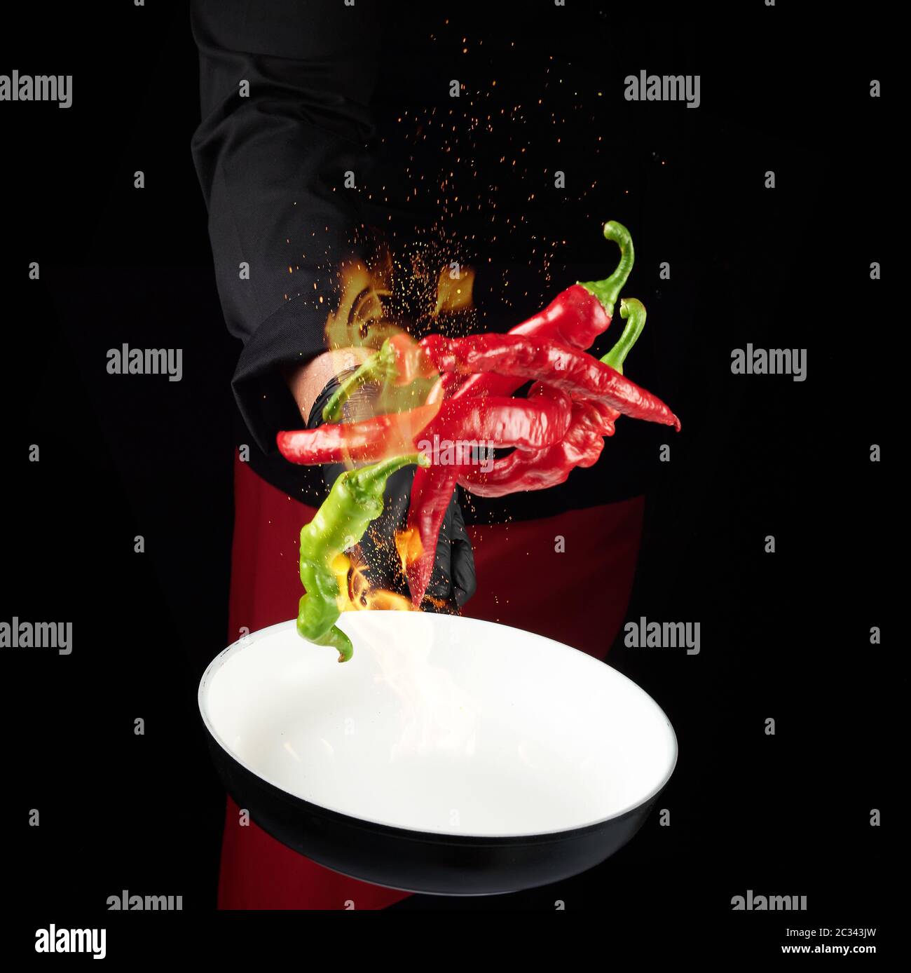 chef in a black uniform holds a round pan and throws up red and green ...