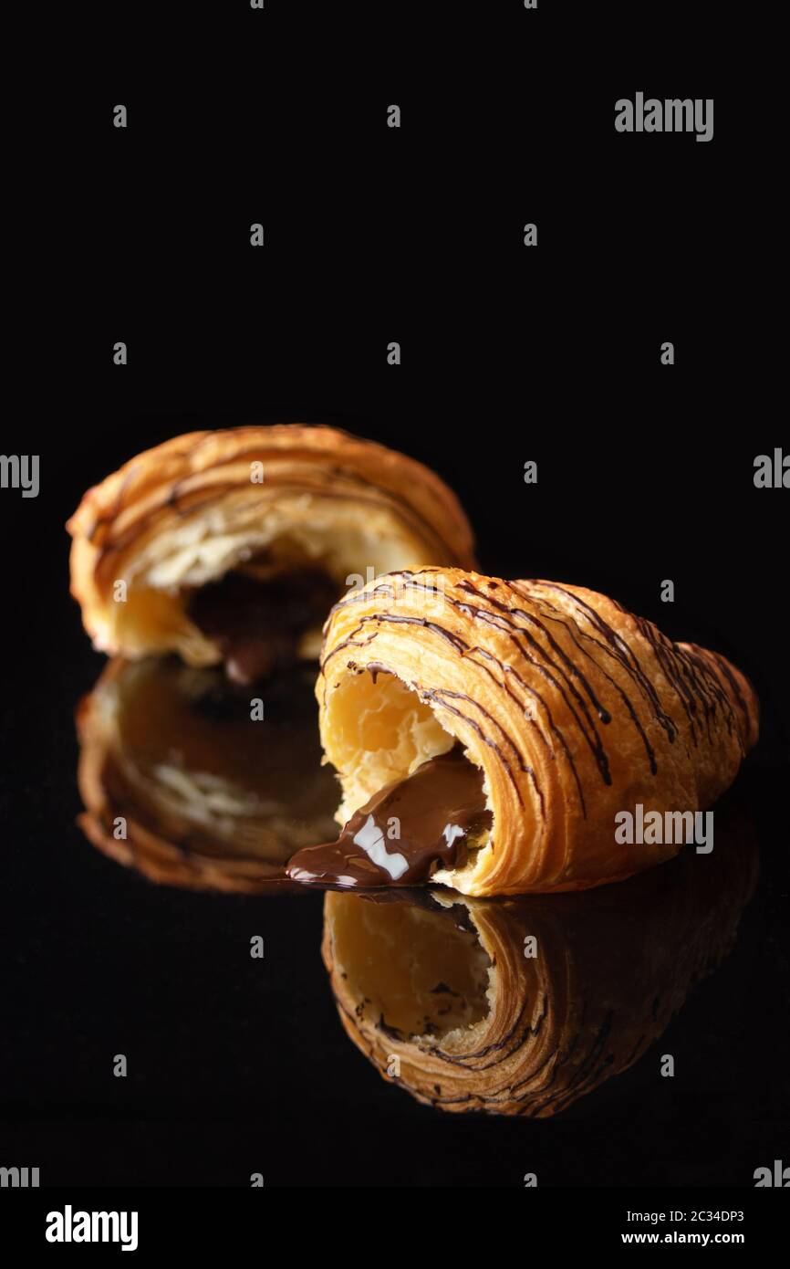 Croissant with chocolate flowing out on a black glass elegant ...