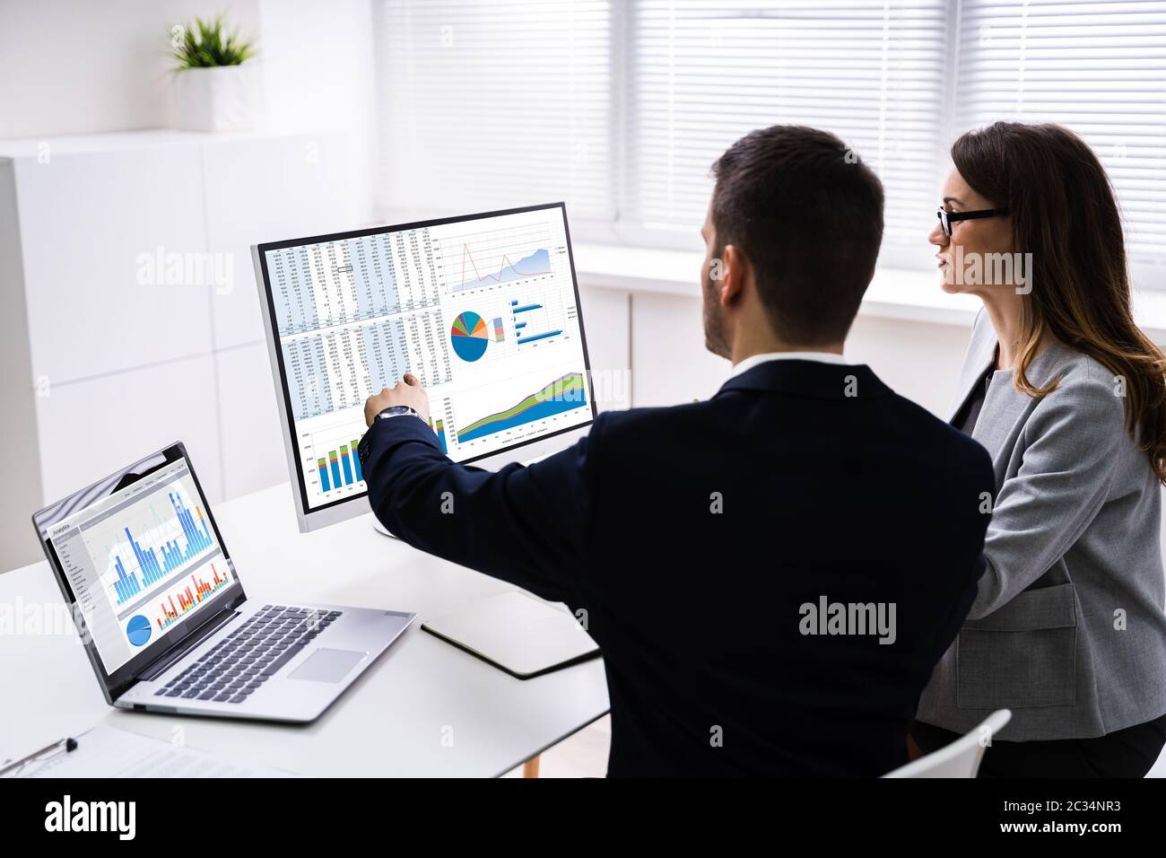 Two Businesspeople Examining Graph On Computer At Workplace Stock Photo ...