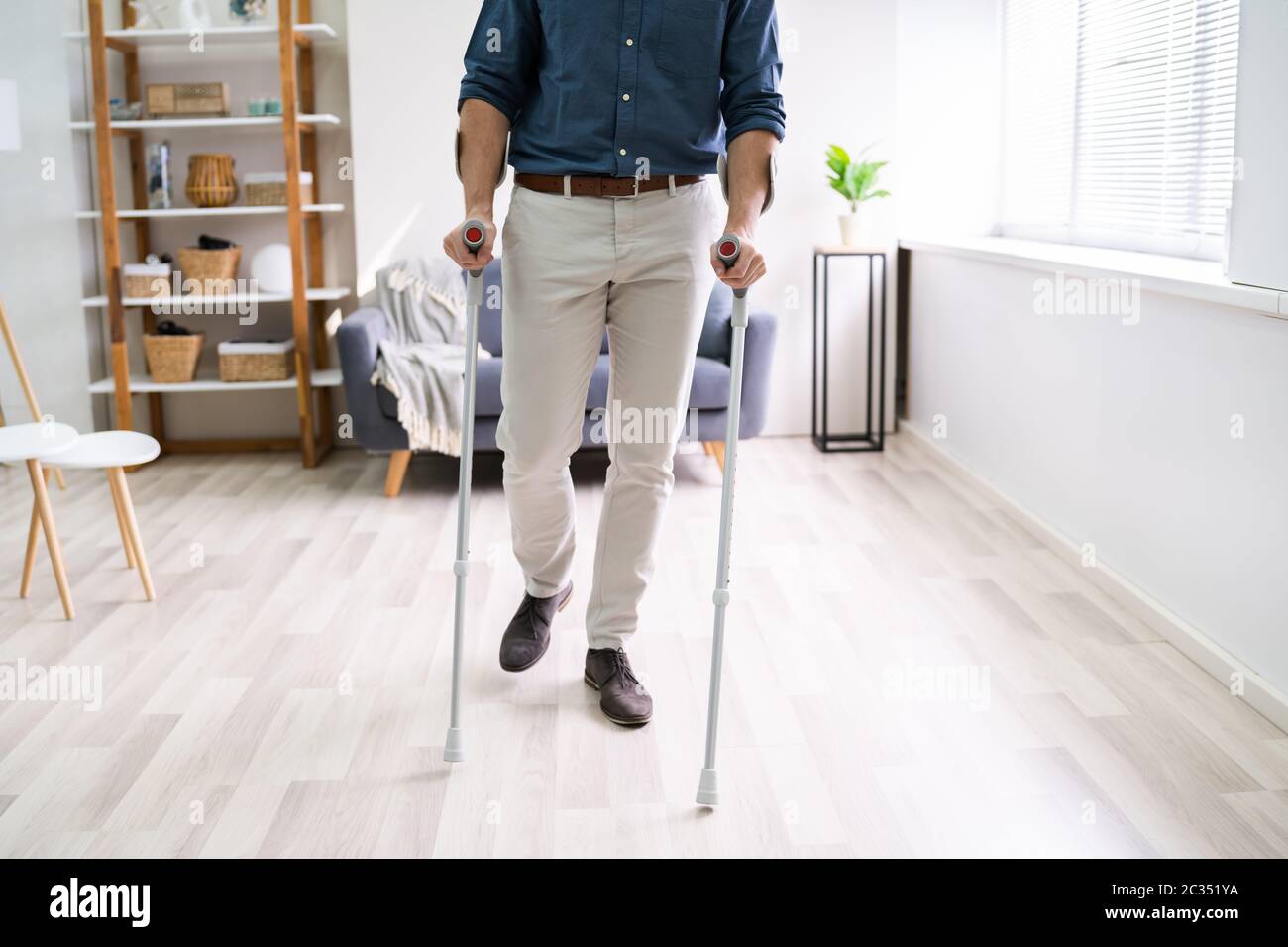 Disabled Man Using Crutches To Walk At Home Stock Photo - Alamy