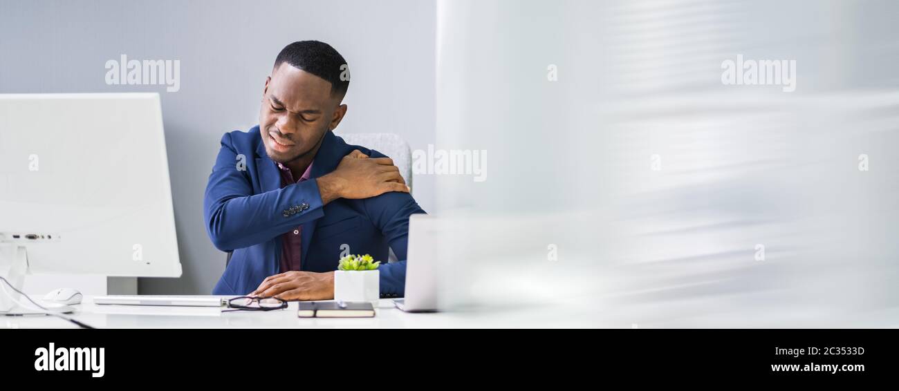 Young Businessman Having Shoulder Pain While Working At Computer Desk ...