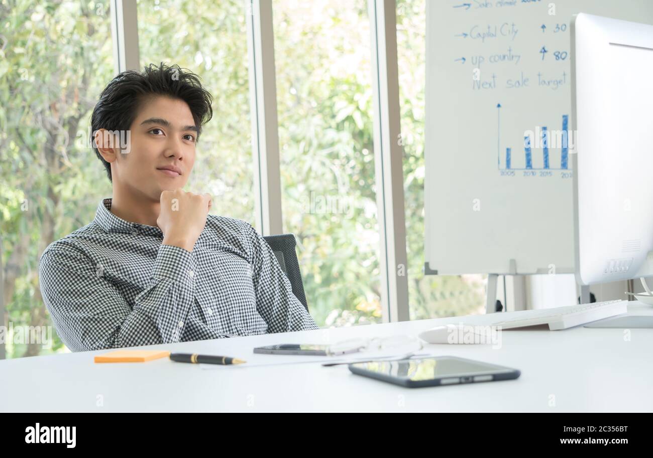 The handsome Asian executive aged 25-35 is sitting at the desk. He is ...