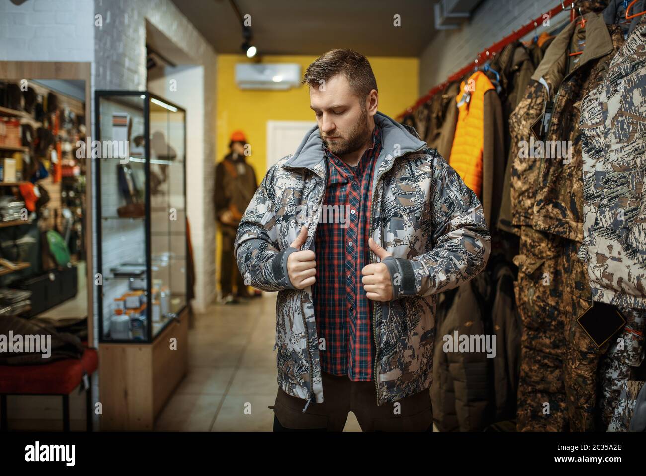 Man trying on uniform at showcase in gun shop. Euqipment and rifles for ...