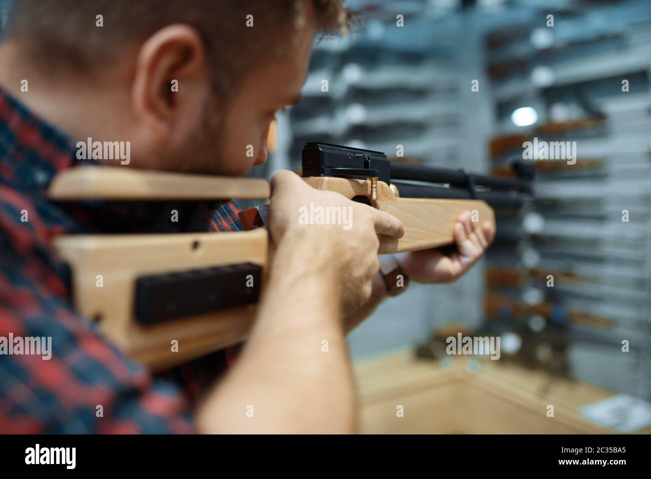 Male person with pneumatic rifle at showcase in gun shop. Euqipment for ...