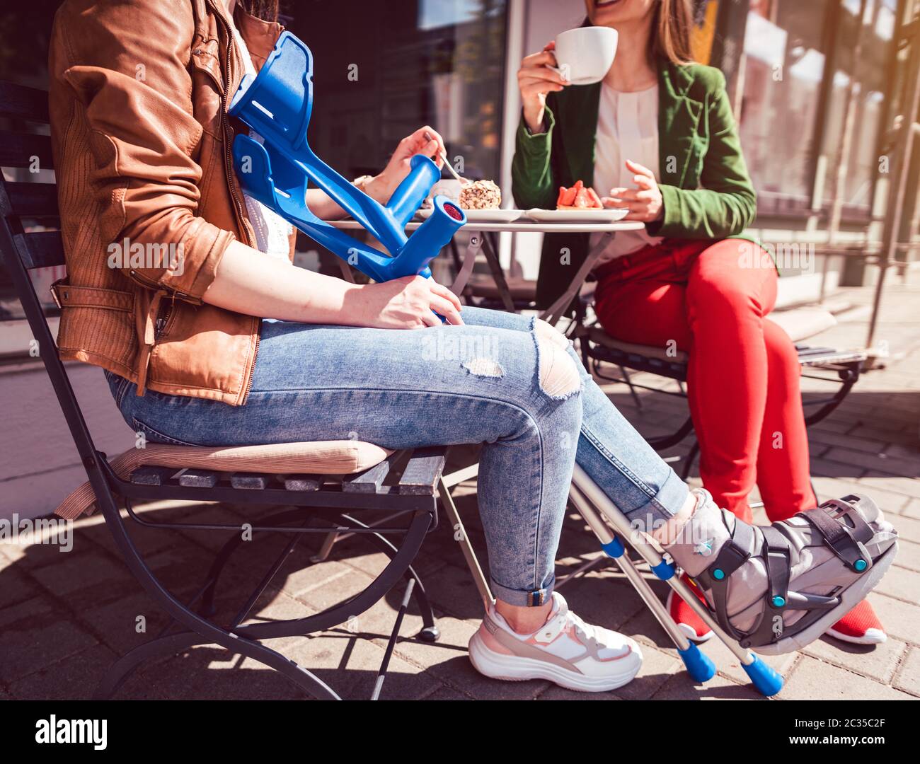 Two women, one with a broken leg and crutches, in a cafe having coffee ...