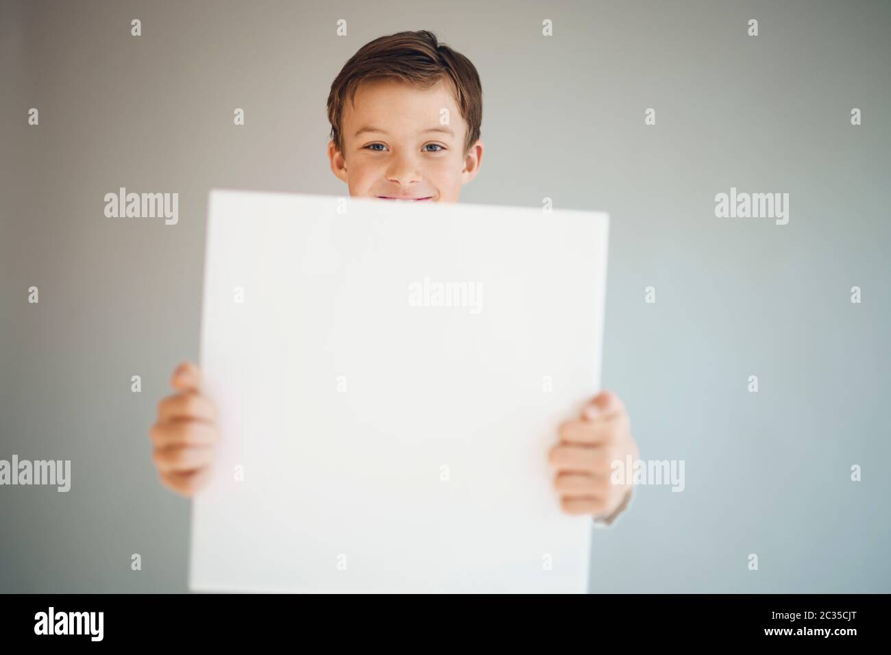 cool young boy holding white sign in front of grey background during ...