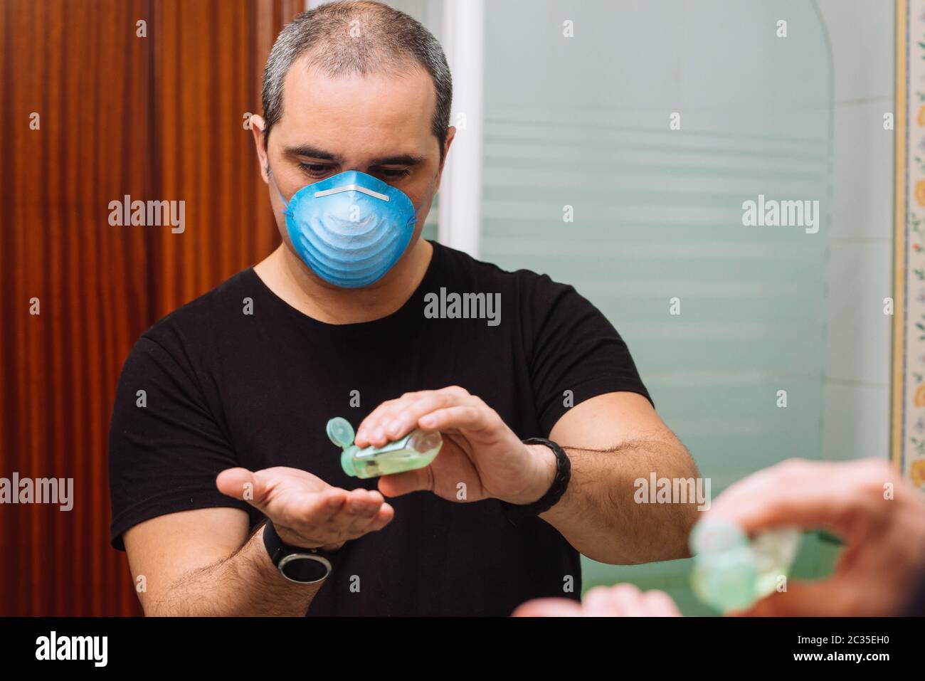 man with face mask applying disinfectant sanitizer onto hand for ...