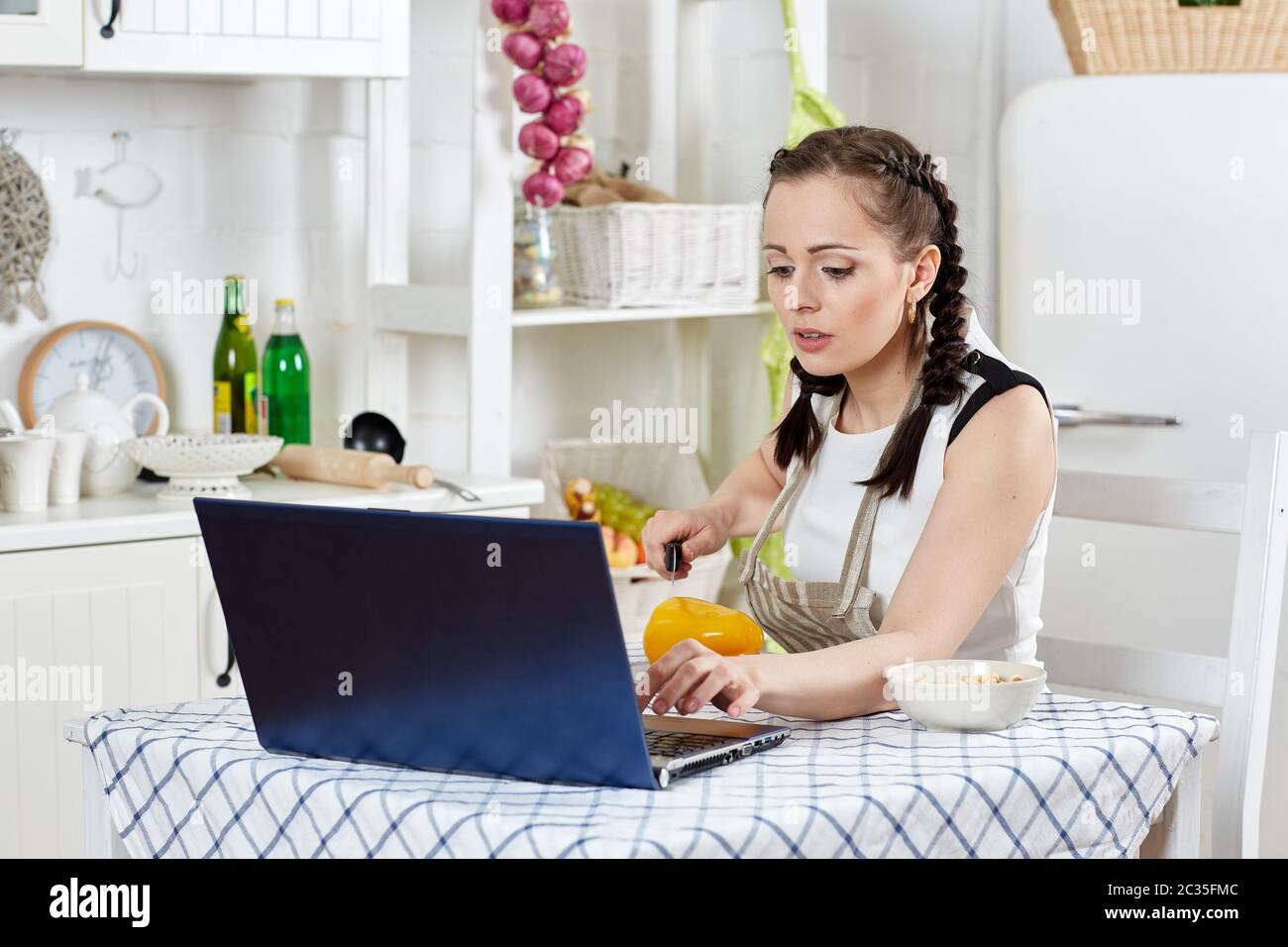 Woman in an apron with notebook cooks in the kitchen. Isolation period ...