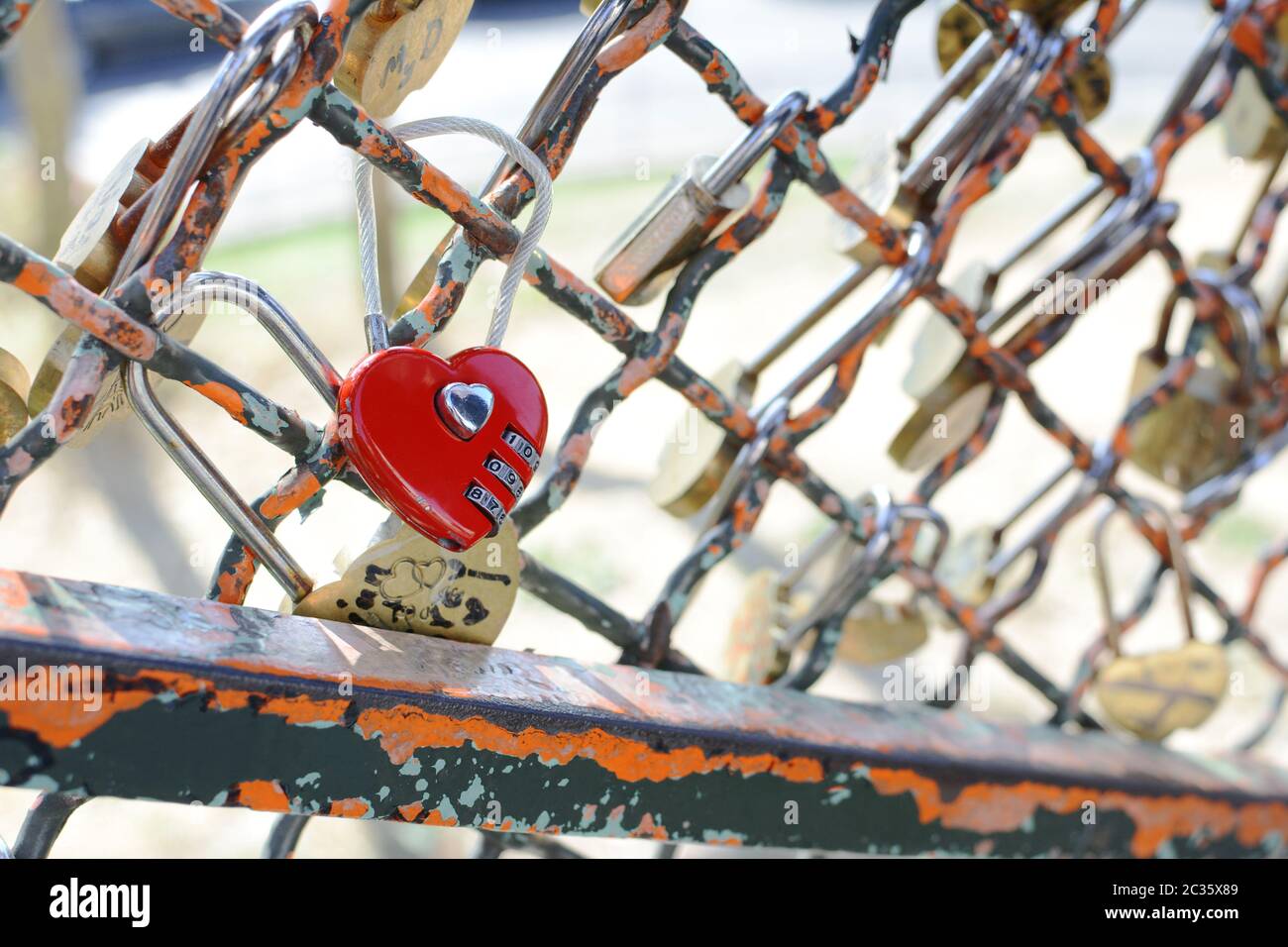 Red heart-shaped combination padlock fastened to metal fence near the ...