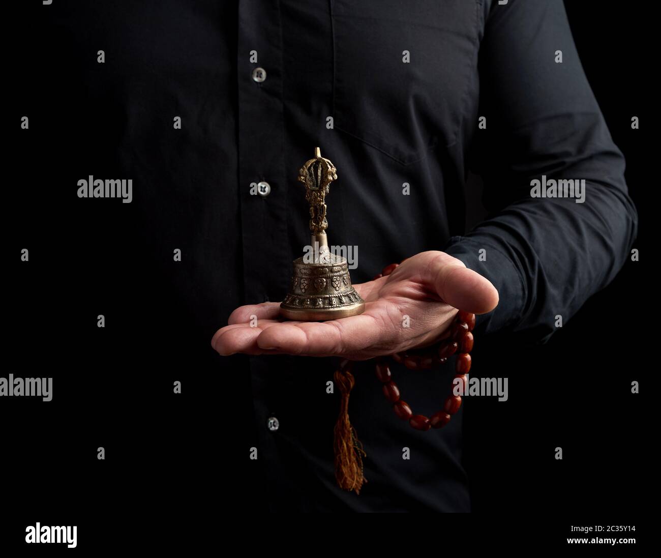adult man in a black shirt holds a copper Tibetan ritual bell, low key ...