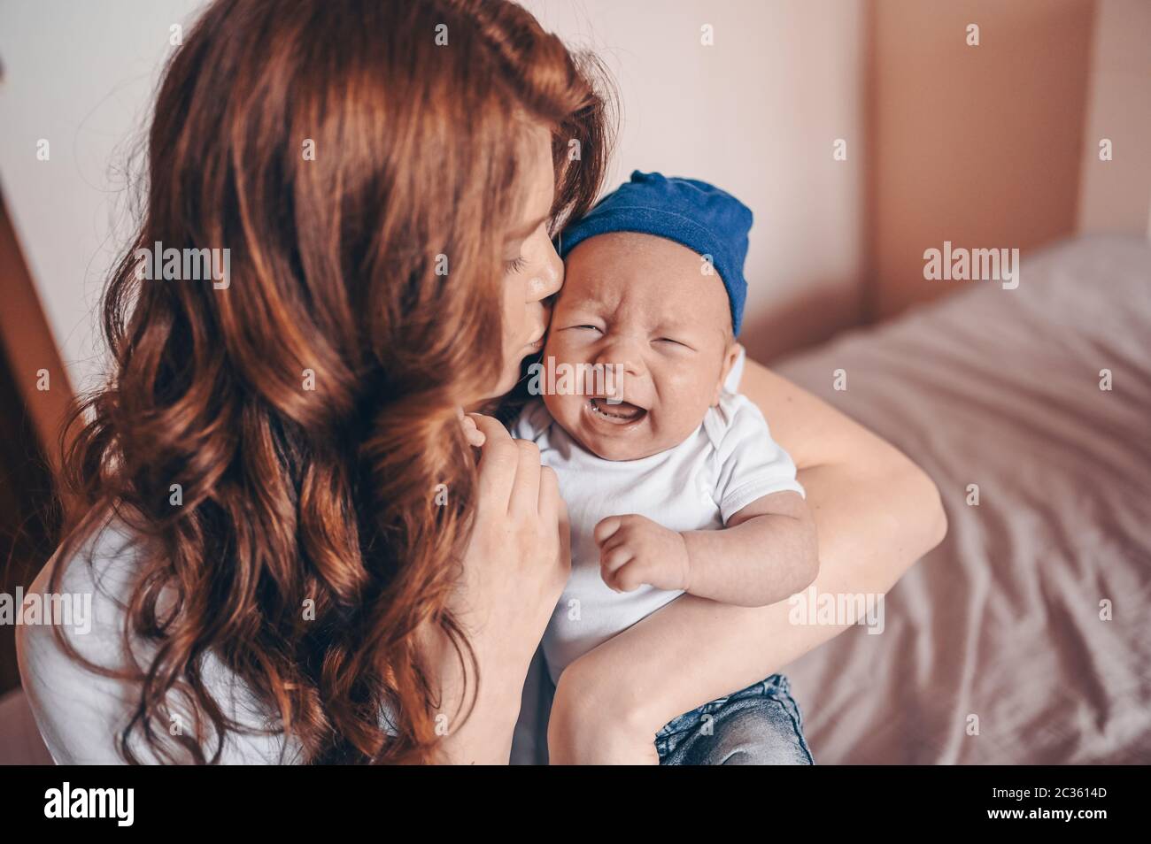 Close up portrait of happy young mom holding her crying baby in blue ...