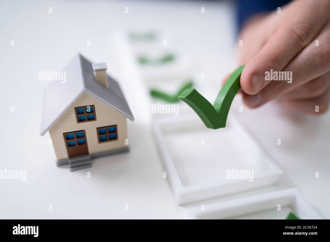 Person's Hand Placing Check Mark Sign Near The House Model On Desk ...