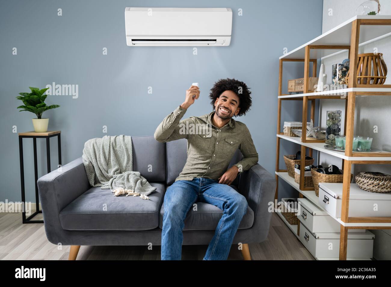 Young Happy Man Sitting On Couch Operating Air Conditioner With Remote ...