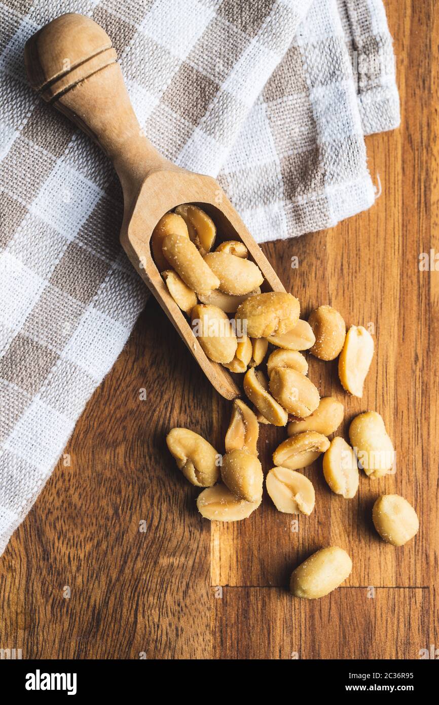 Roasted salted peanuts. Crispy nuts in scoop on wooden table. Top view ...