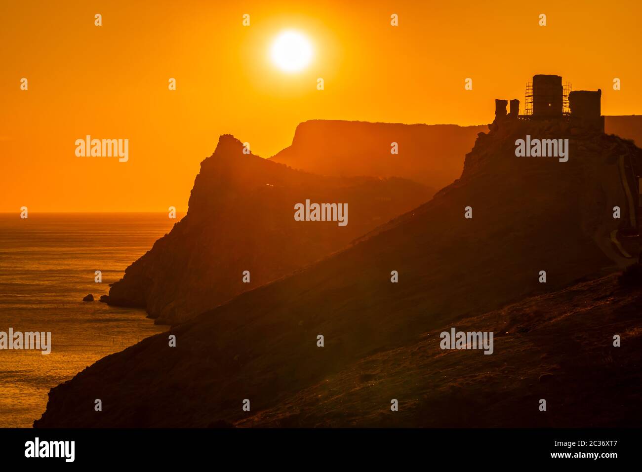 A red burning sunset with the silhouette of a cliff and old castle over ...