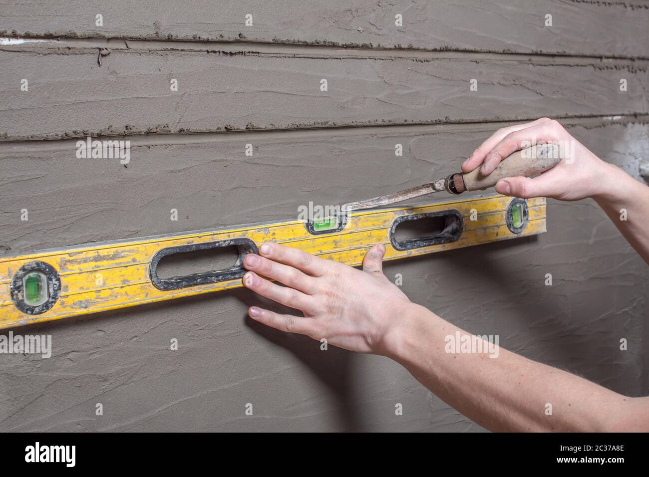 The hand draws horizontal stripes of embroidery on the plaster. The ...