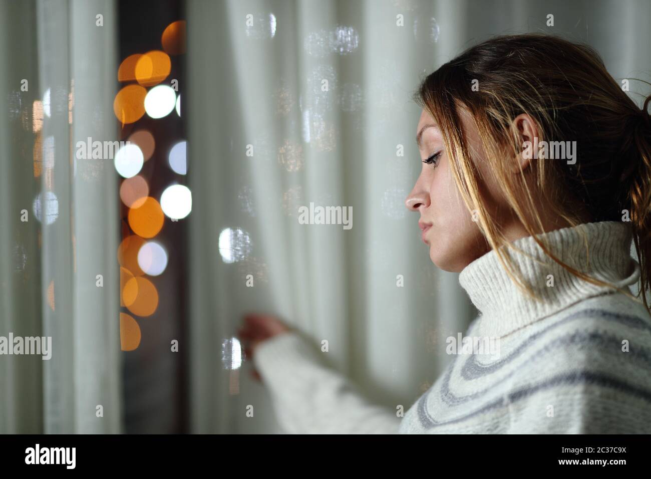 Sad woman alone complaining standing looking at city lights through a ...