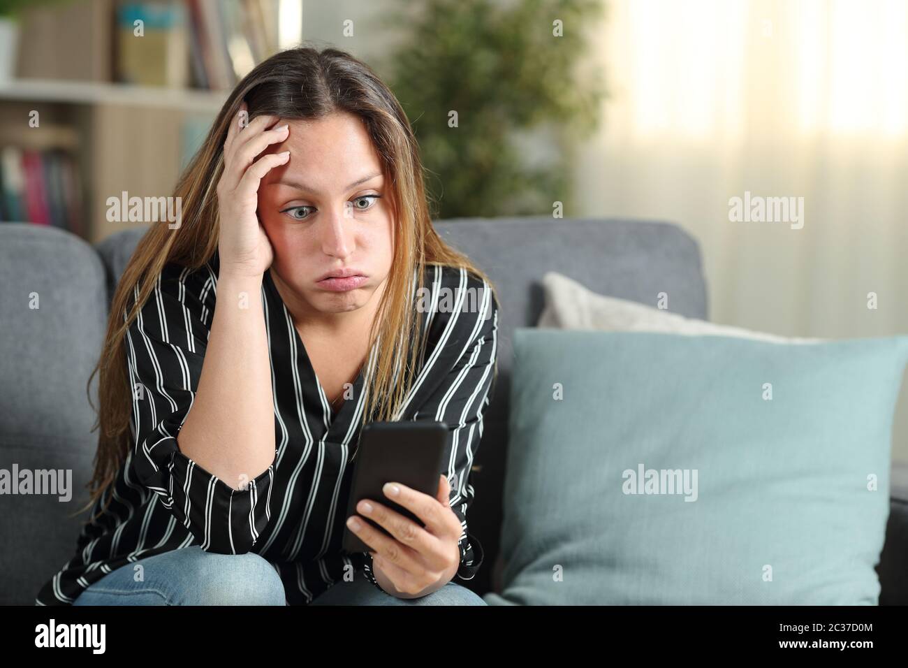 Frustrated woman reading complicated mobile phone content sitting on a ...