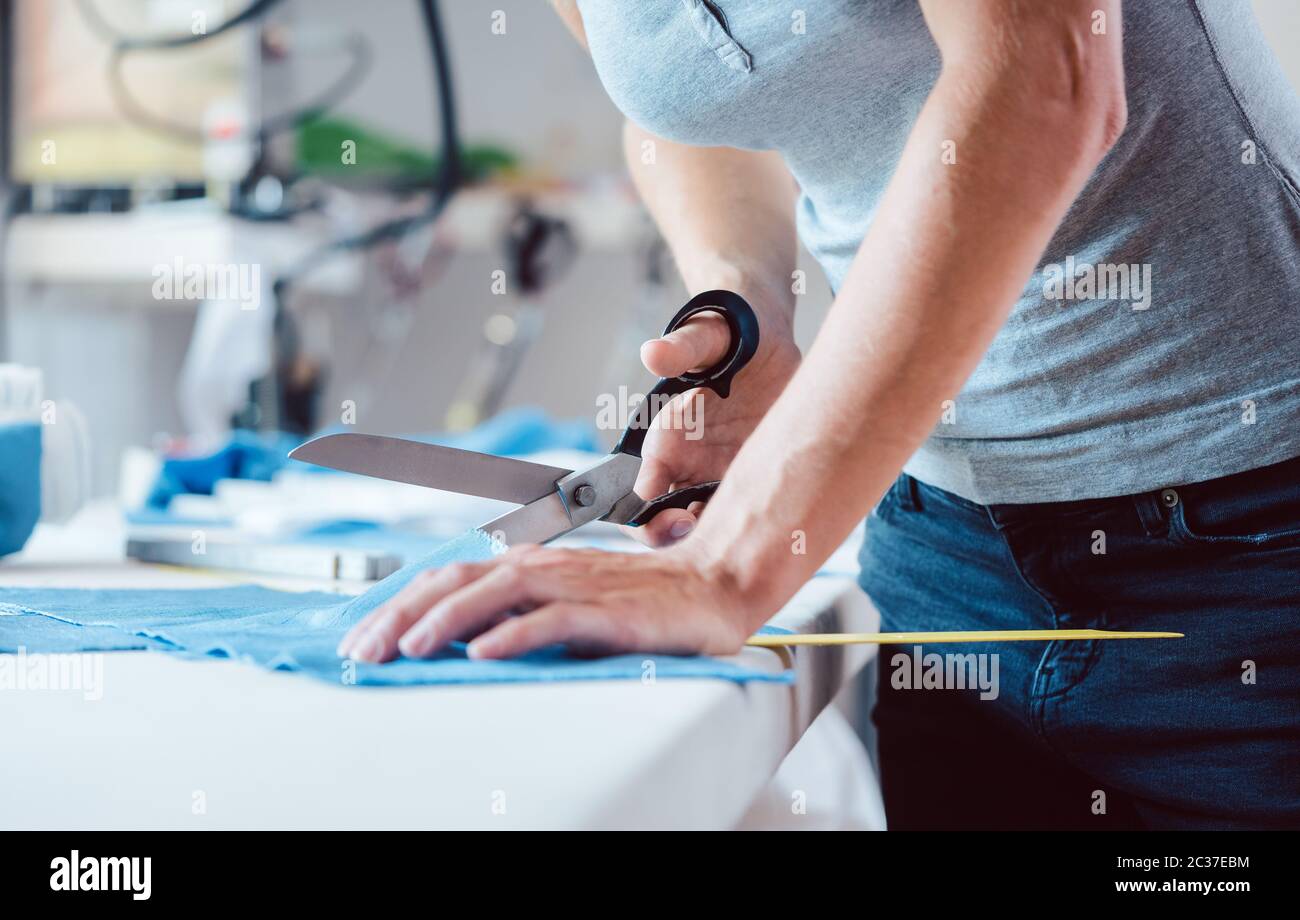 Woman cutting fabric with tailor scissors on tailor's table in a studio ...