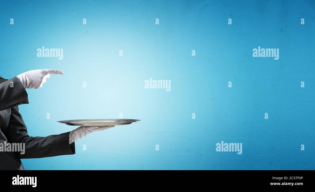 Hand of butler holding empty metal tray against blue background Stock ...
