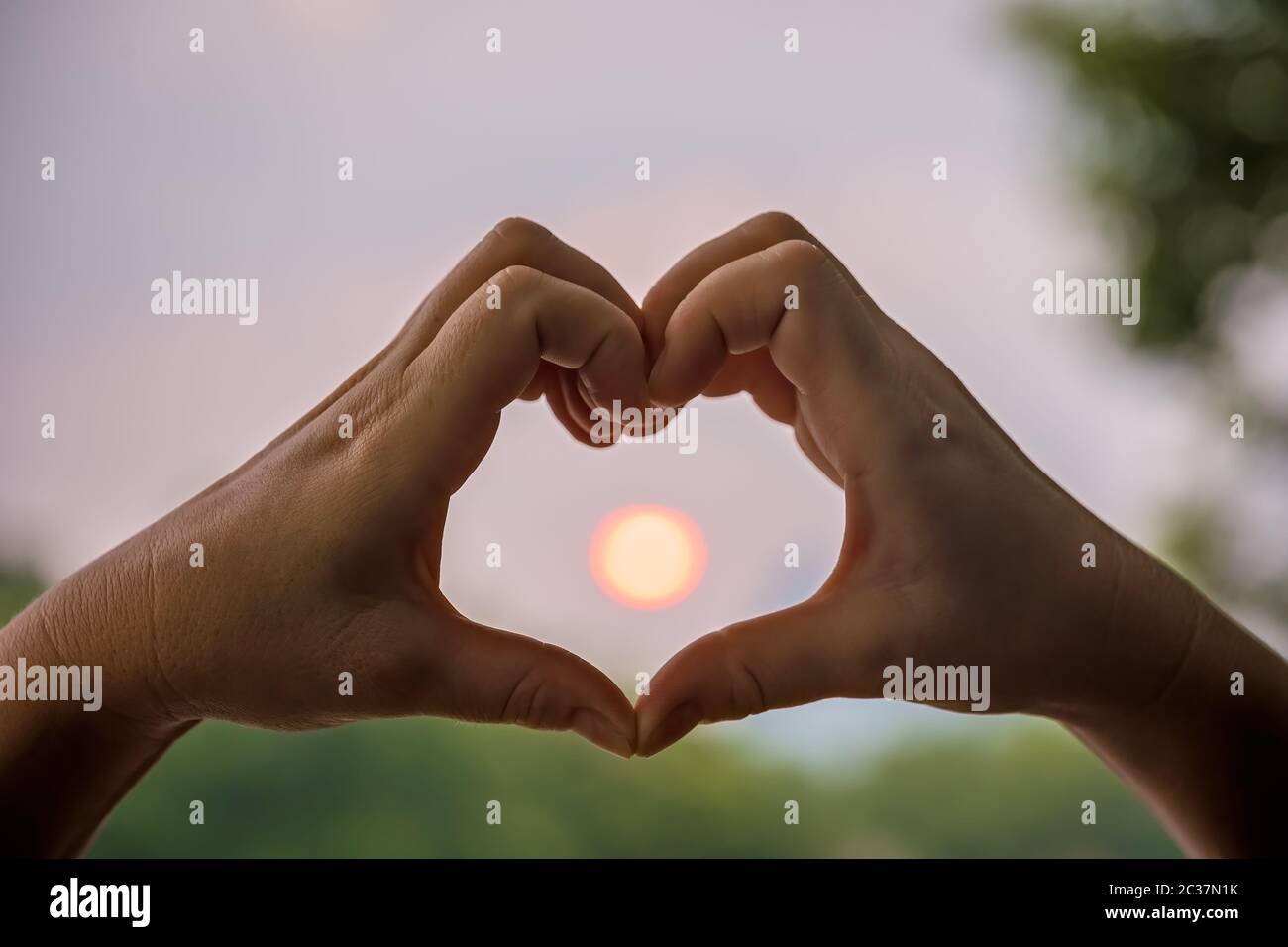 Womans hands catching sun while making heart shape at dusk Stock Photo ...