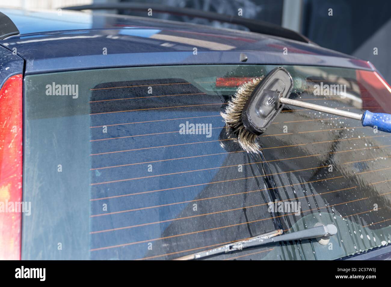 hand wash the rear window of the car using brush and water with shampoo ...