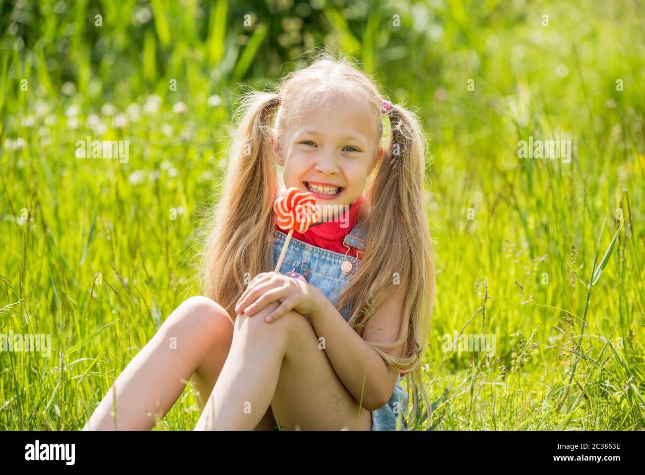 Blonde little girl with long hair and candy on a stick Stock Photo - Alamy