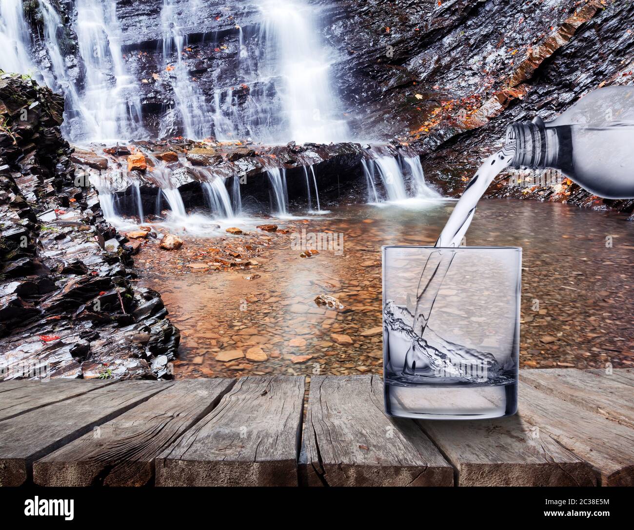 Water flowing from a bottle into a glass against a waterfall background ...