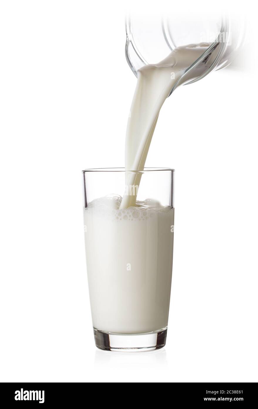 Milk pouring into a glass from glass jug isolated on white background ...