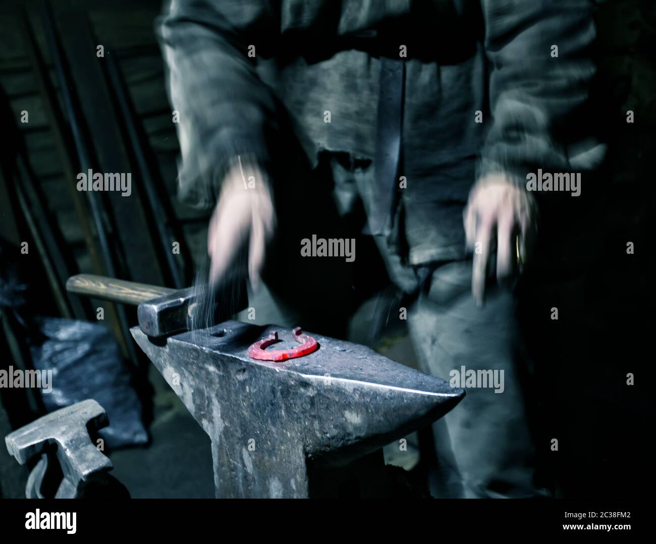 Hands of a blacksmith with a hammer blowing a warmed horseshoe. The ...