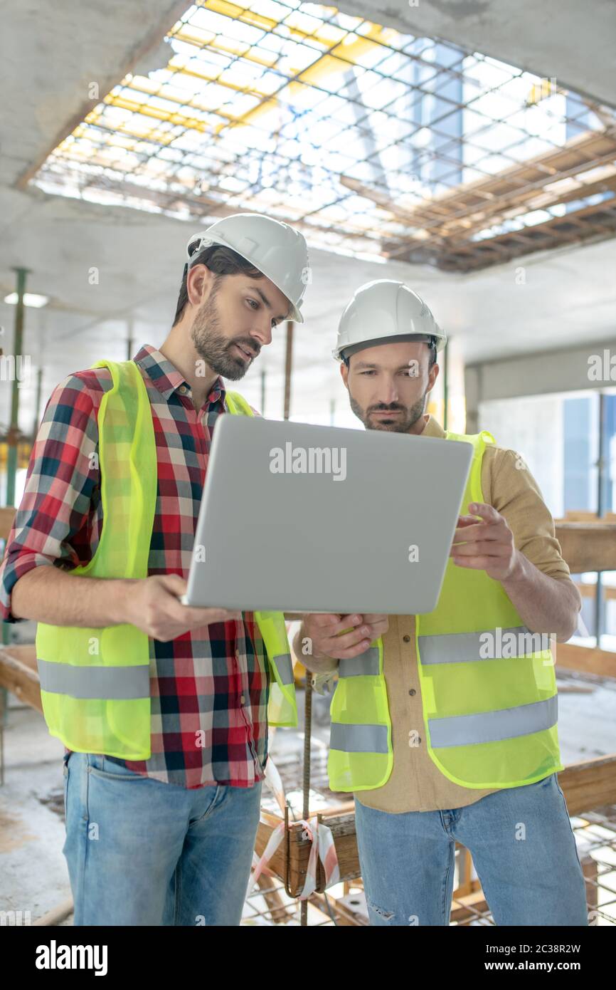 Building site. Building workers in yellow vests holding laptop ...