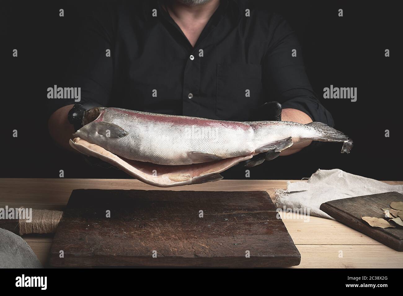 chef in a black shirt and black latex gloves holds a raw carcass of ...
