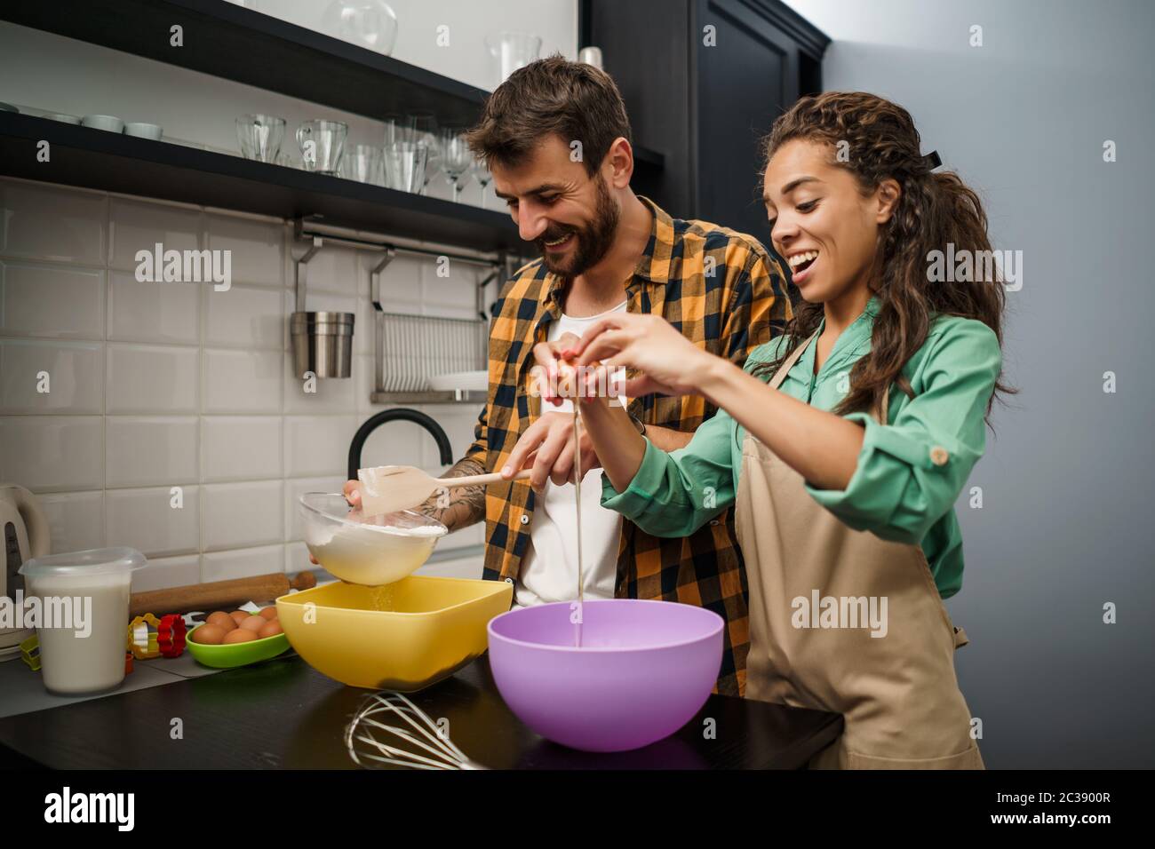Happy multiethnic couple cooking in their kitchen. They are making ...