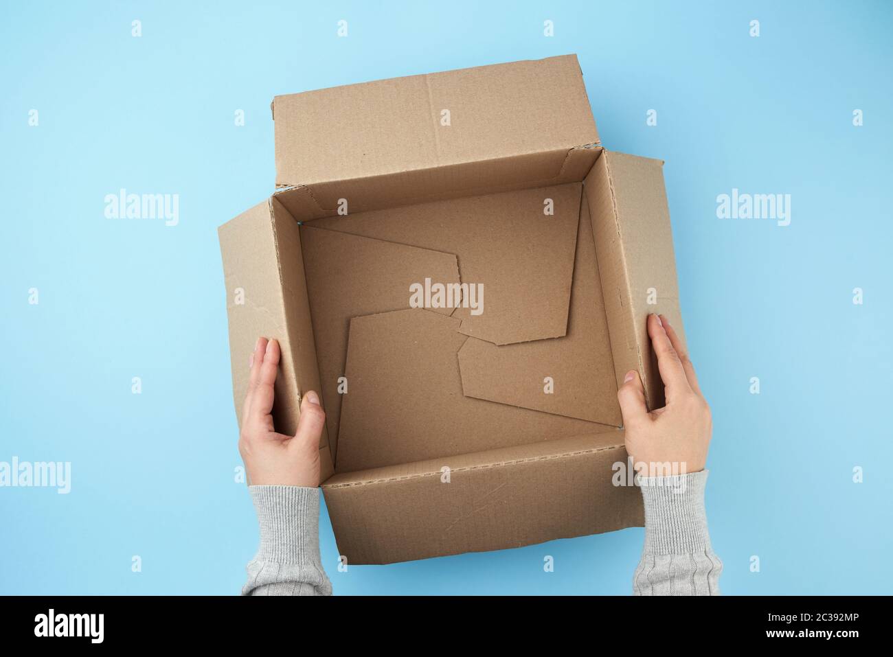 two female hands are holding an empty open box of brown cardboard, top ...