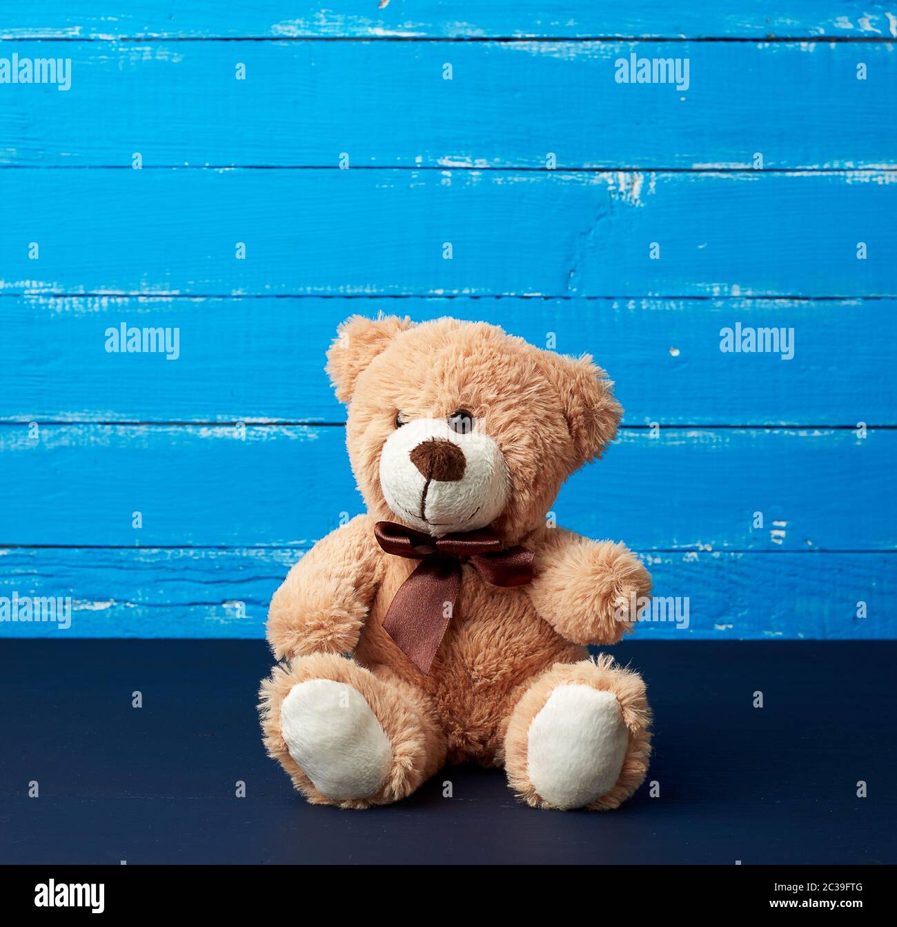 beige teddy bear sitting on a blue wooden background, place for an ...