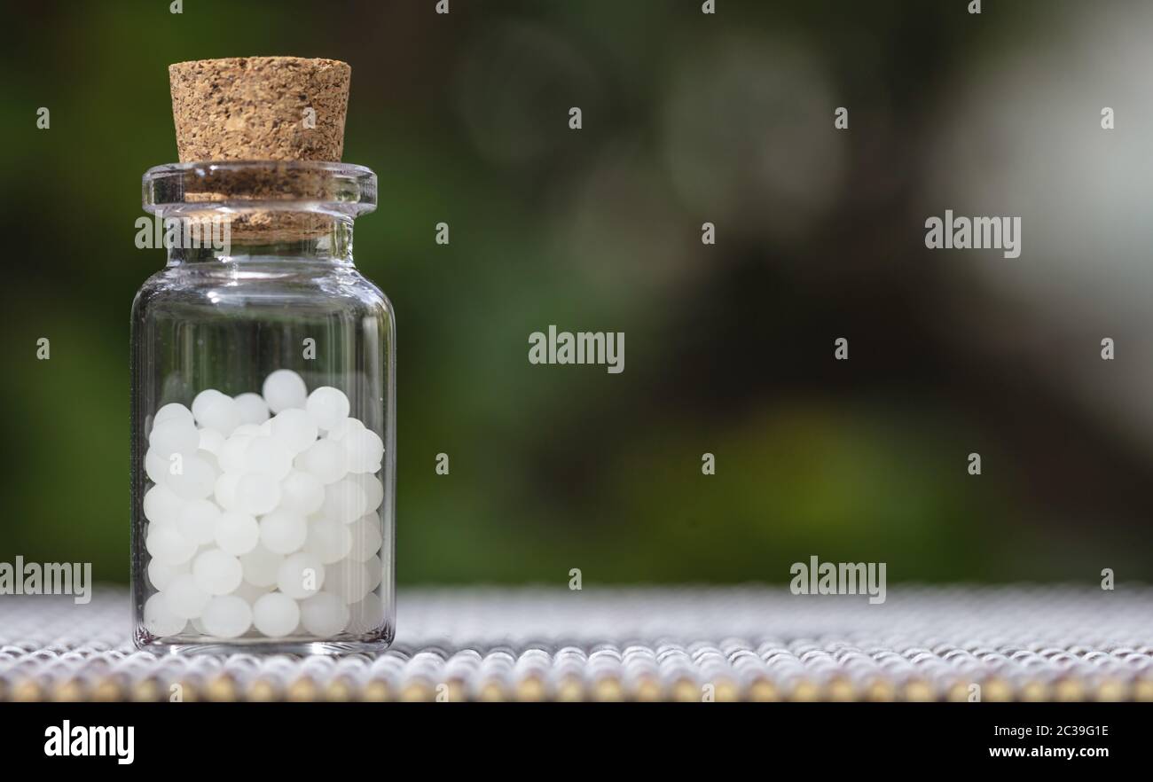 Homeopathy, globules in a clear glass bottle, green nature background ...