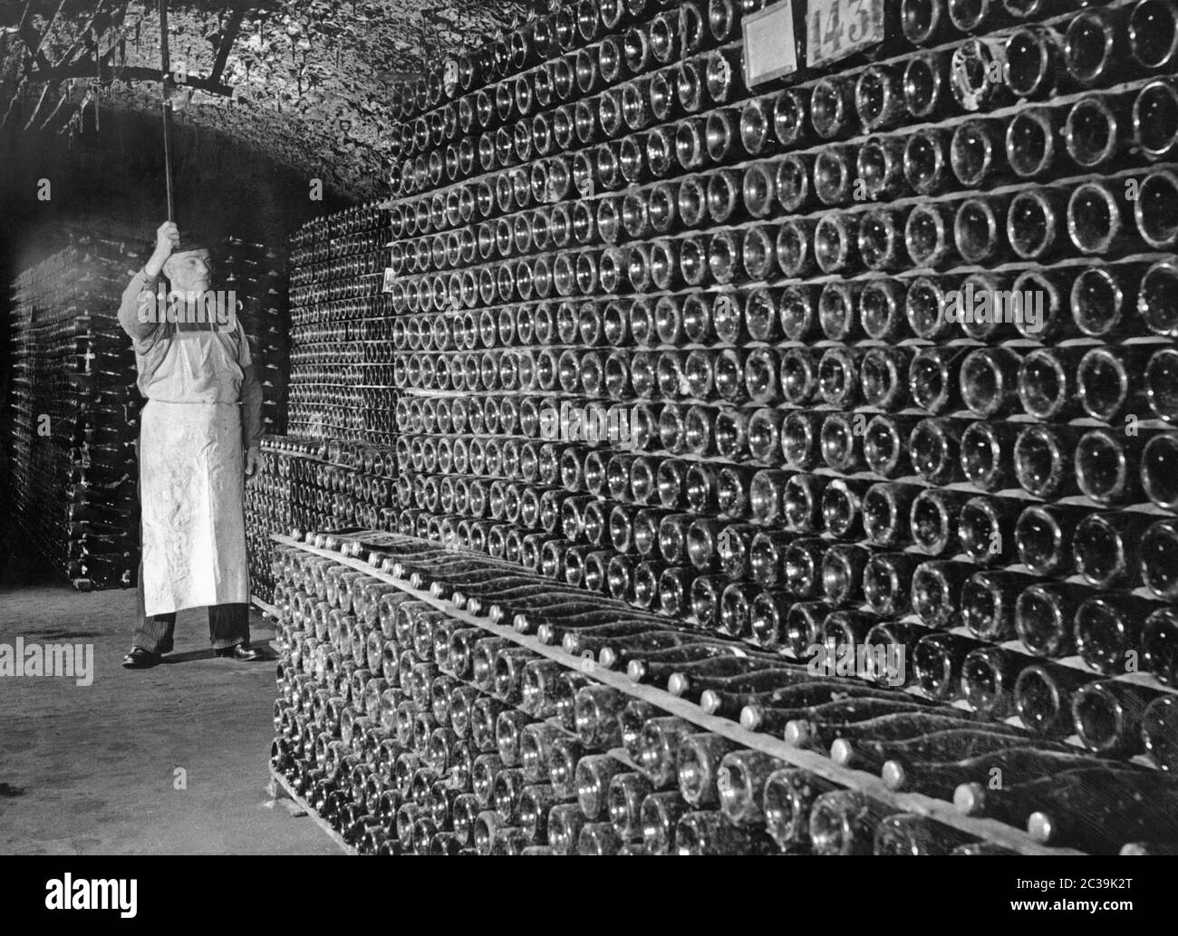 A winemaker stands in a wine cellar in front of shelves with wine ...