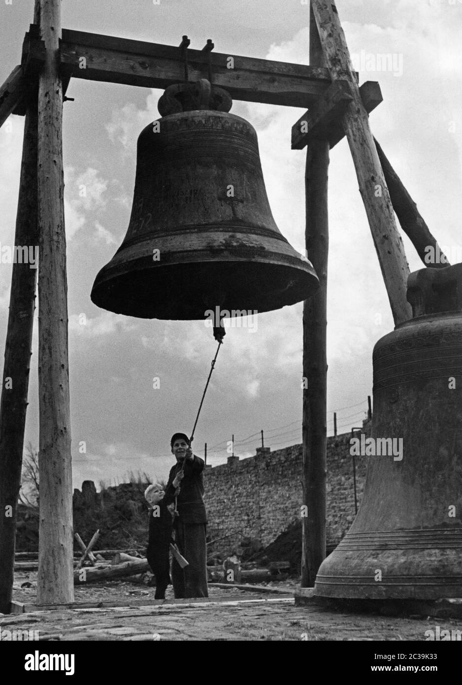 A child rings a big bell with the help of an adult. On the floor there ...